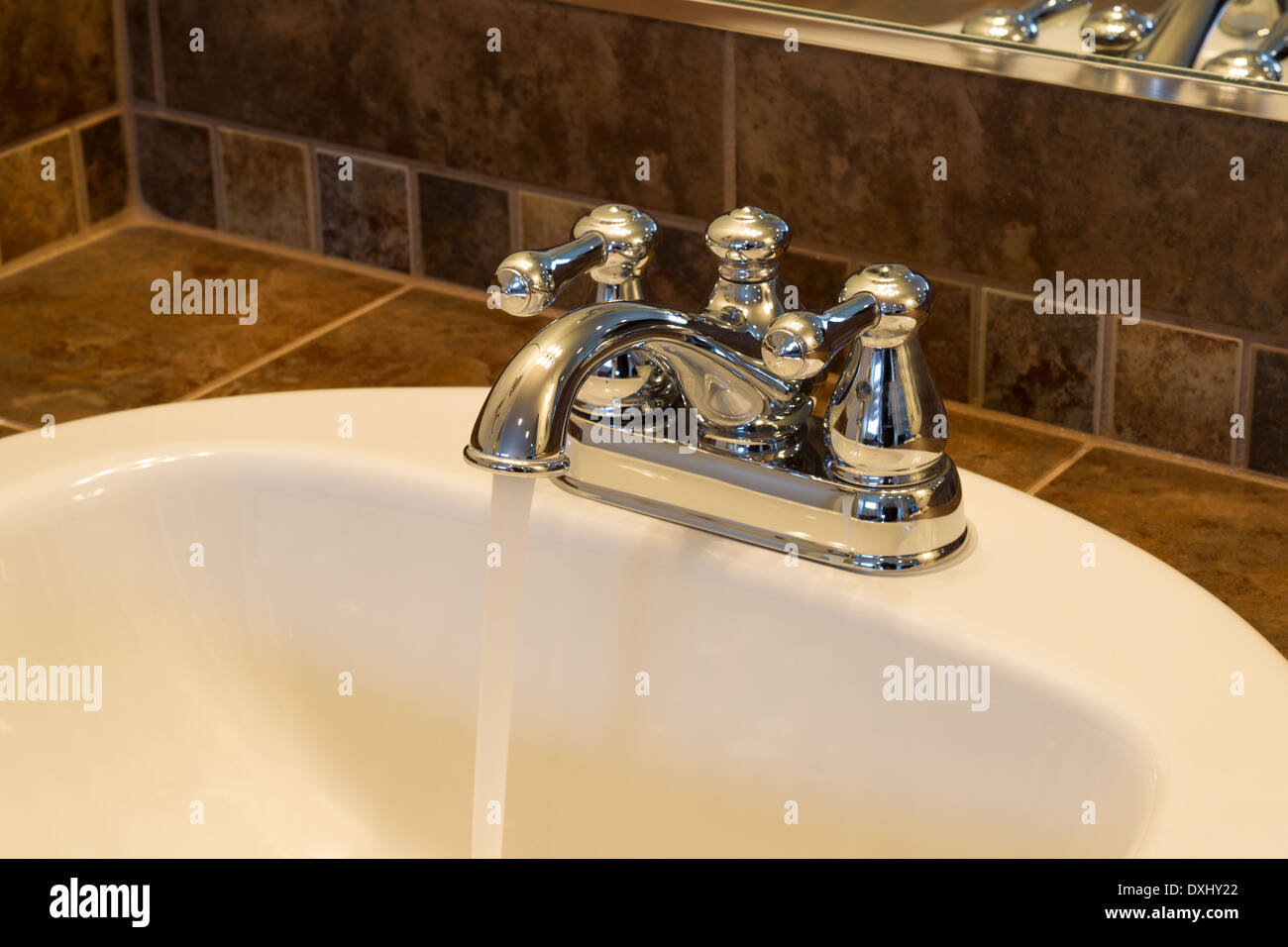 Horizontal photo of chrome faucet running water into bathroom sink with ...