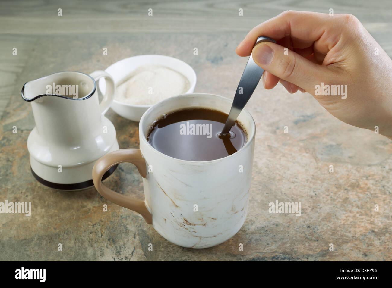 Closeup horizontal photo of female hand stirring cream and sugar with ...