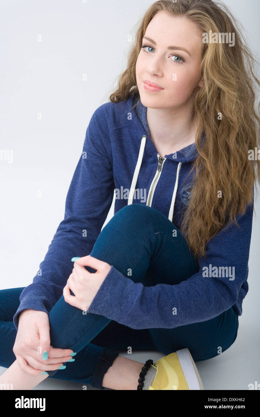 Portrait of a teenage girl sitting crossed legged on a studio floor ...