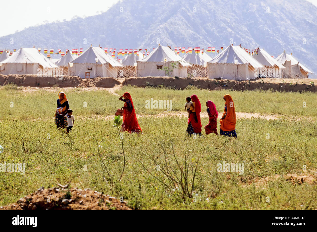 Group of Indian women walking through fields in front of tourist tents ...