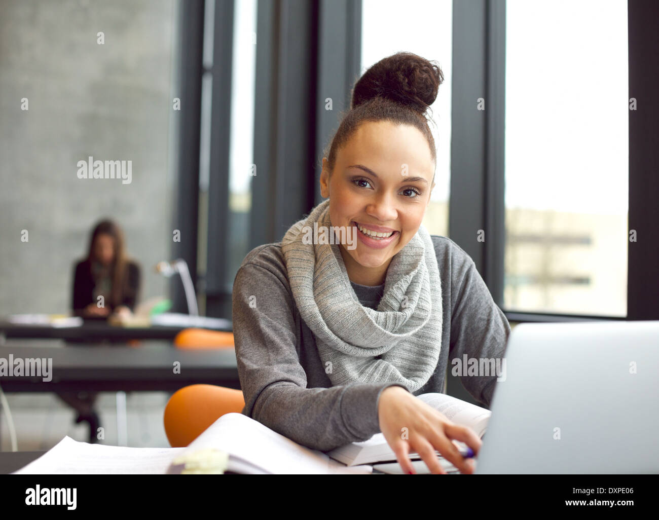 Happy young woman sitting in the library with books and a laptop ...