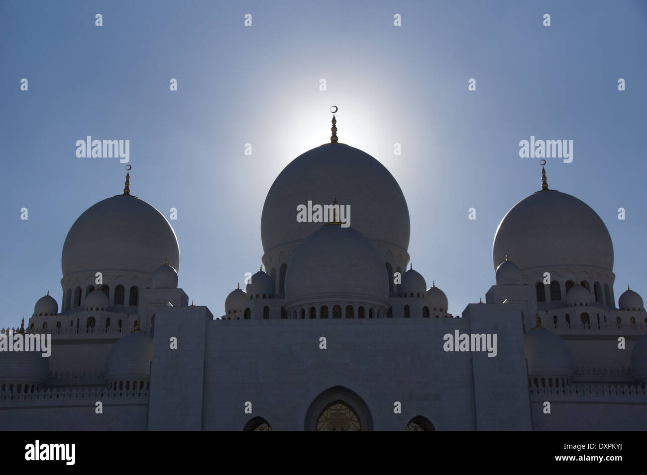 The domes of the Sheikh Zayed Grand Mosque with the sun setting behind ...