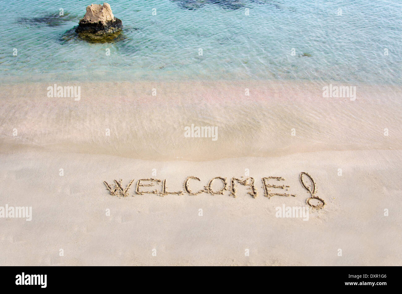 Welcome message written on white sand, with tropical sea waves in ...