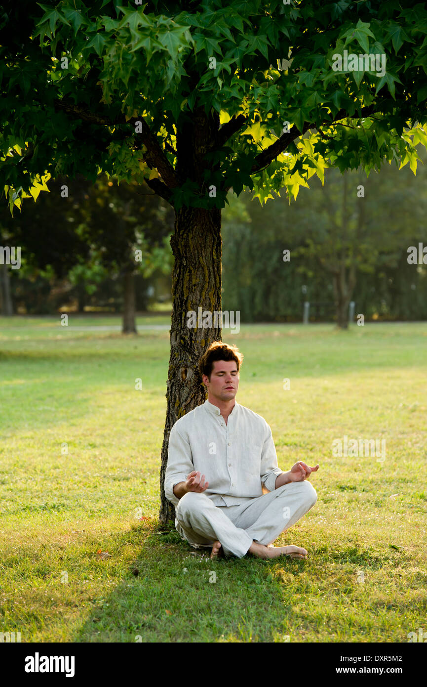 Young man meditating under a tree Stock Photo - Alamy