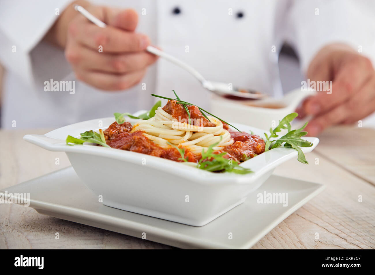 Male chef in restaurant kitchen is garnishing and preparing pasta dish ...