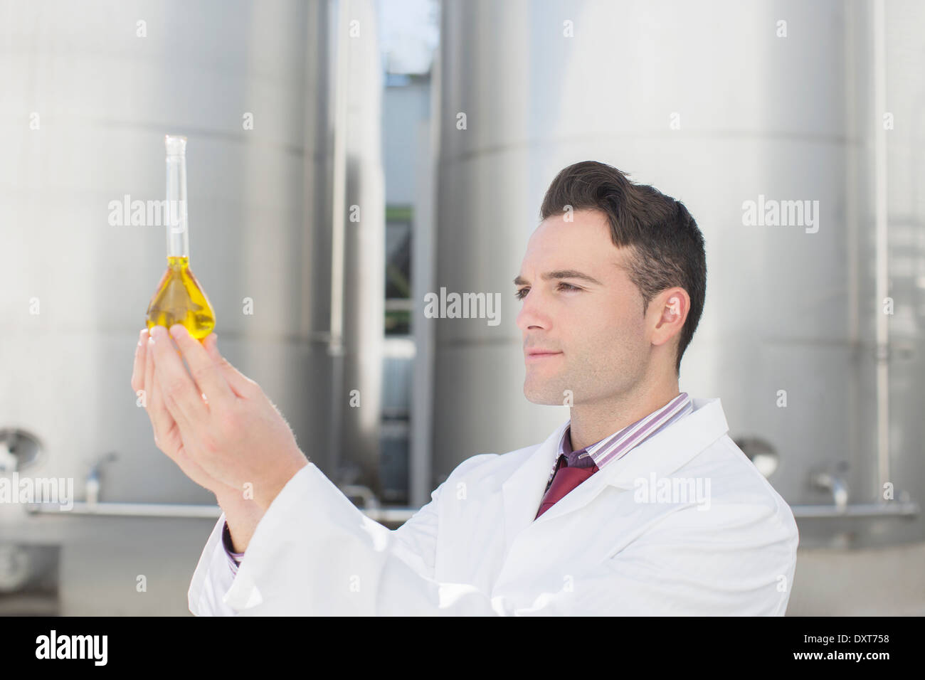 Scientist examining liquid in beaker next to silage storage towers ...