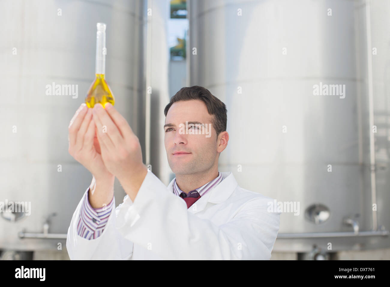 Scientist examining liquid in beaker next to silage storage towers ...