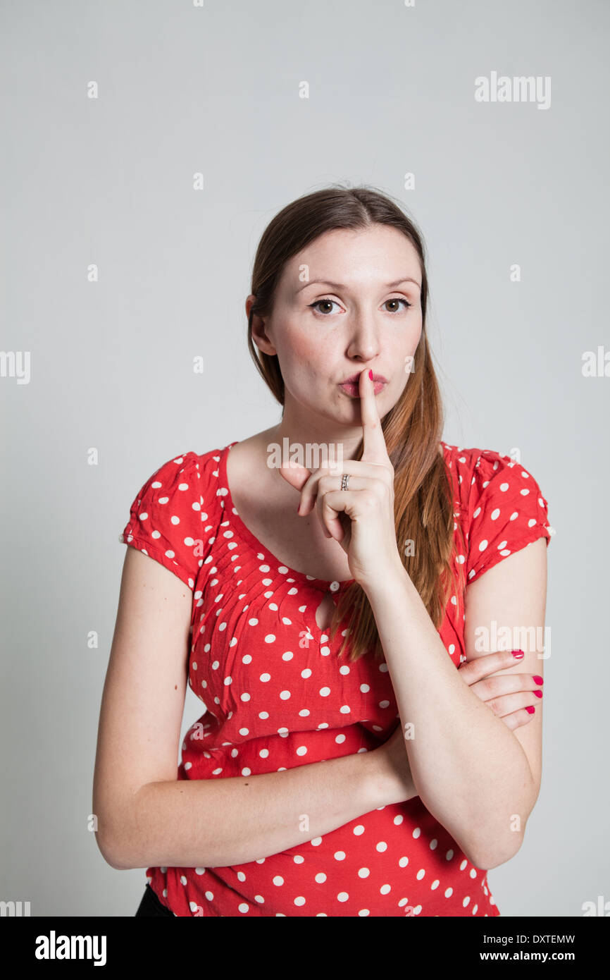 Studio portrait of attractive woman with finger over pursed lips to ...