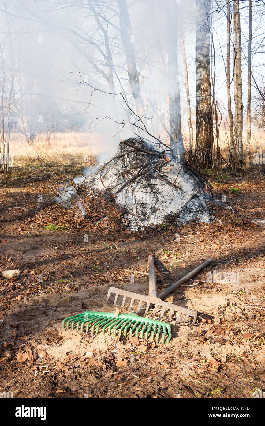 Iron and green plastic rakes on the ground, smoking bonfire in ...