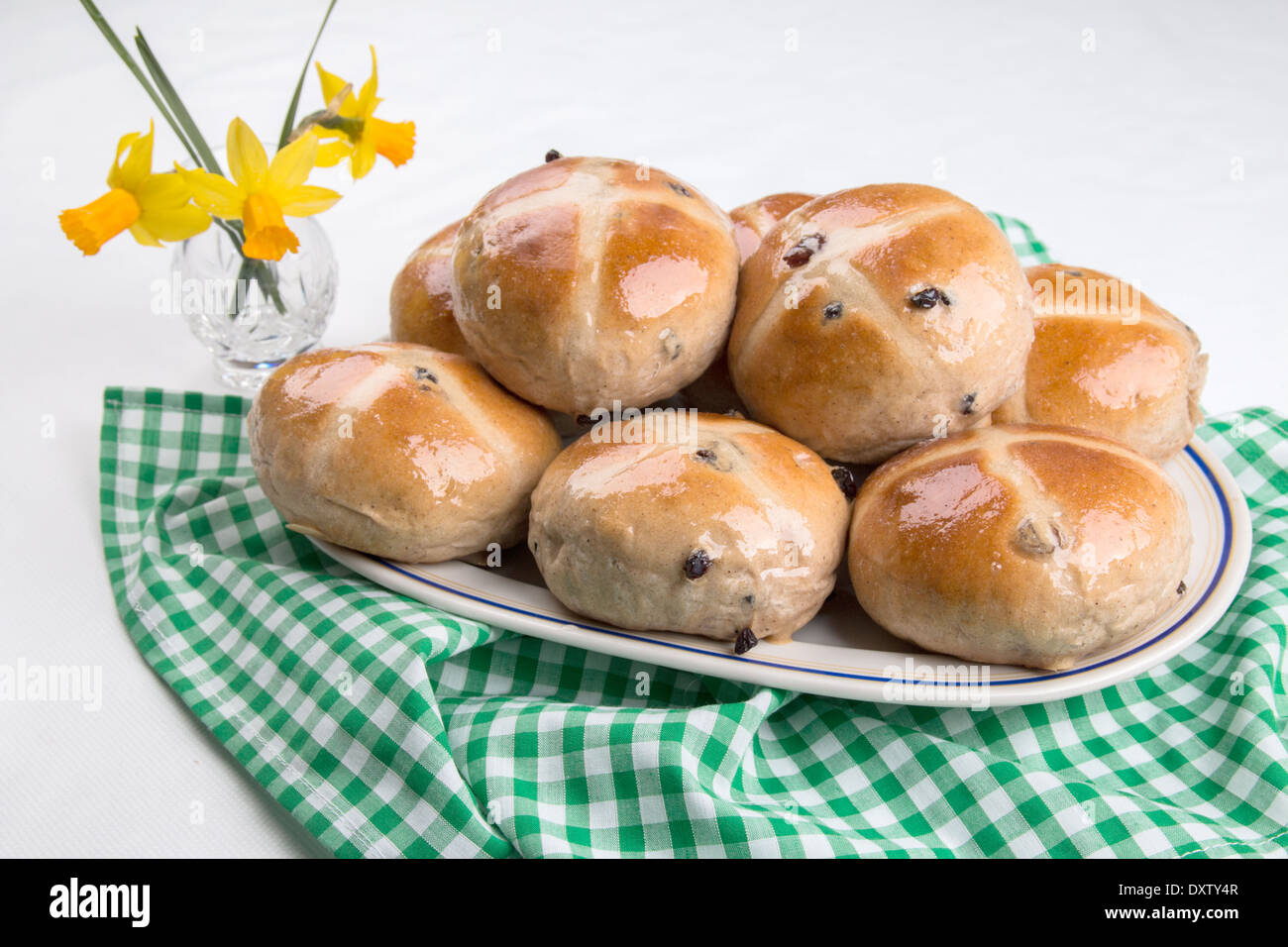 Hot cross buns on a green checked cloth serviette with cut bun on a ...