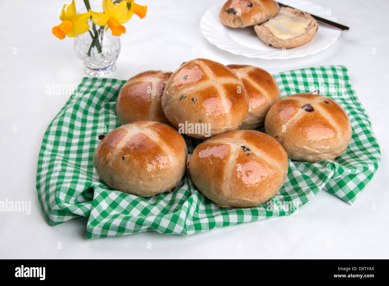Hot cross buns on a green checked cloth serviette with cut bun on a ...