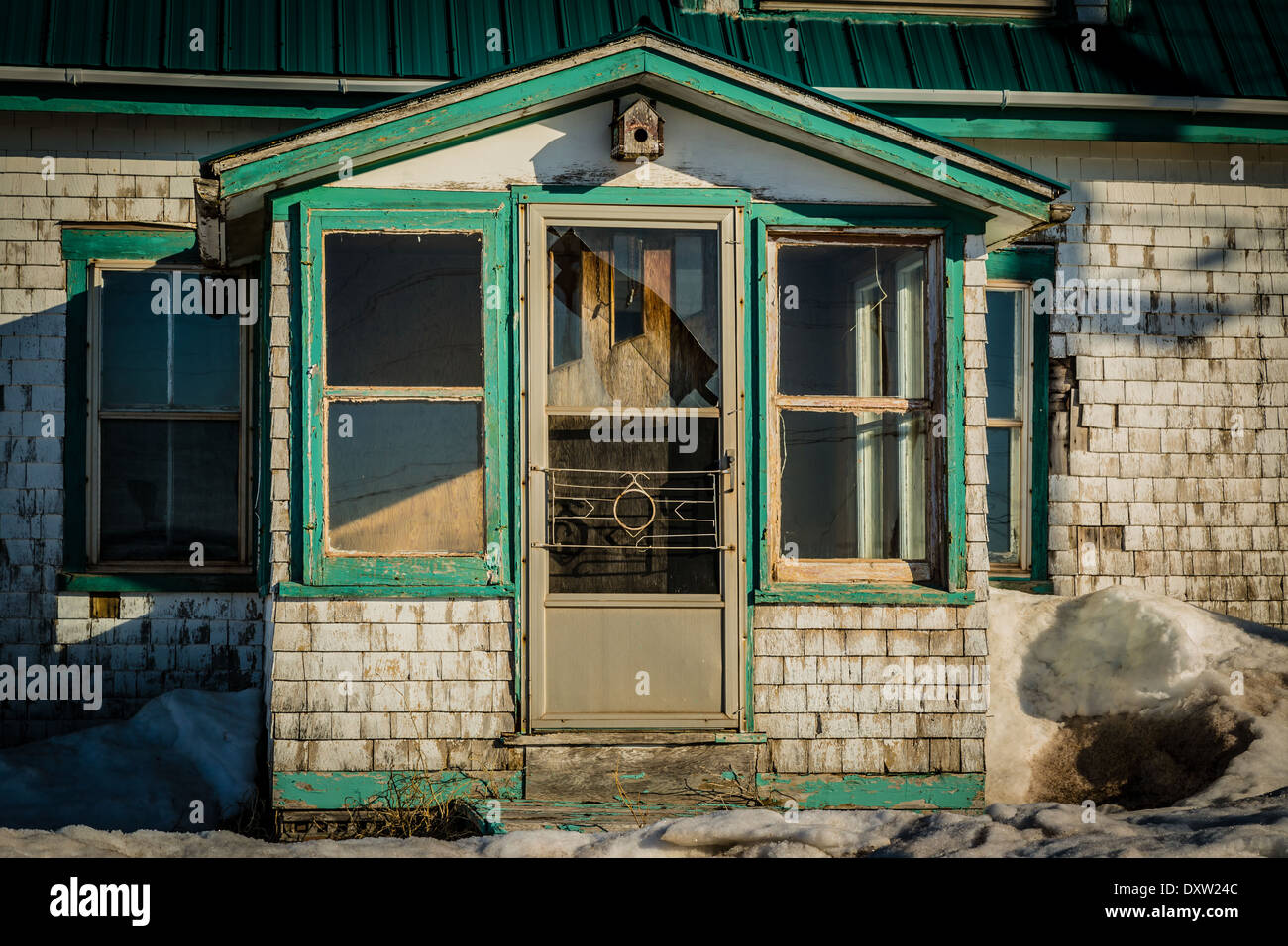 Snow drifts around the front entrance of a deteriorated and abandoned ...