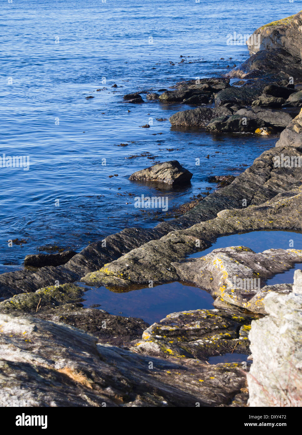 Blue sea and rocks with rockpools, calm sea with small waves on the ...