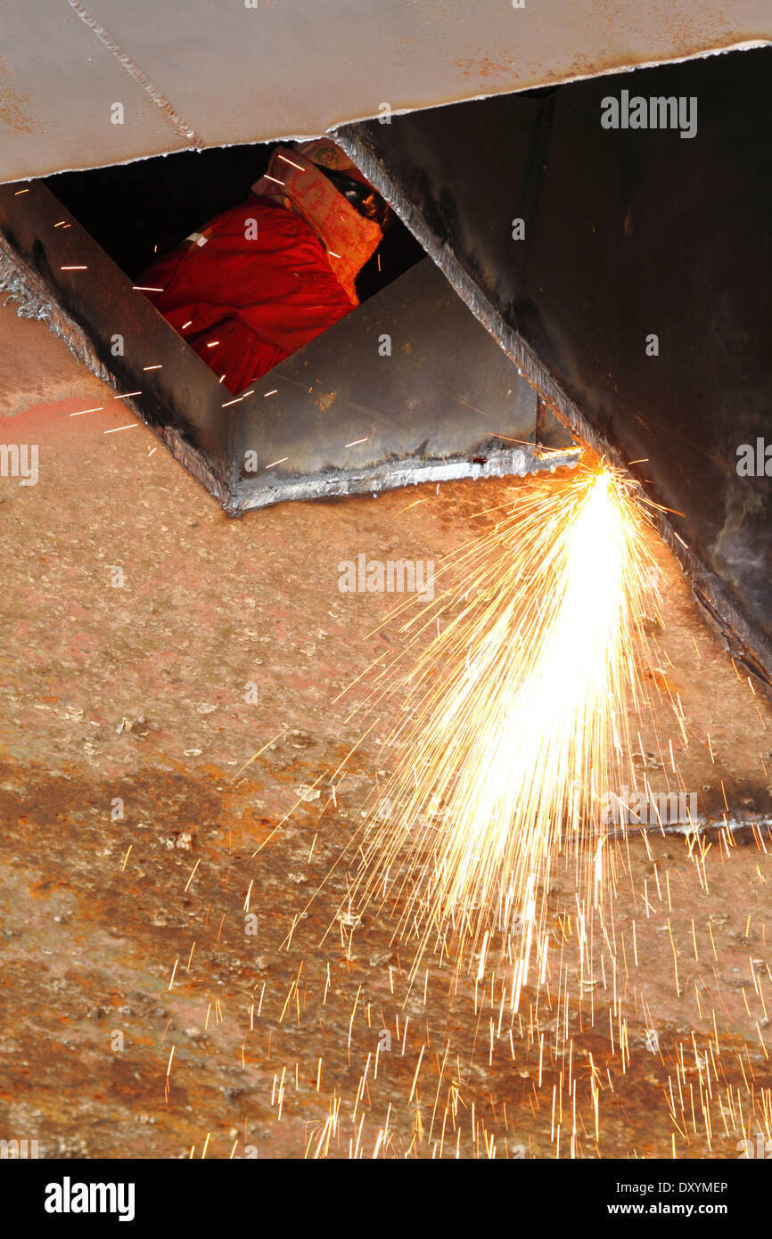 Sparks fly as steel is cut from an old barge by an oxy acetylene torch ...