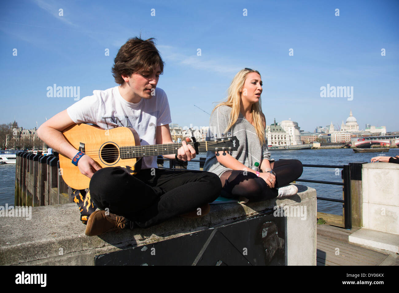 Two young buskers singing and playing guitar on the riverside wall ...