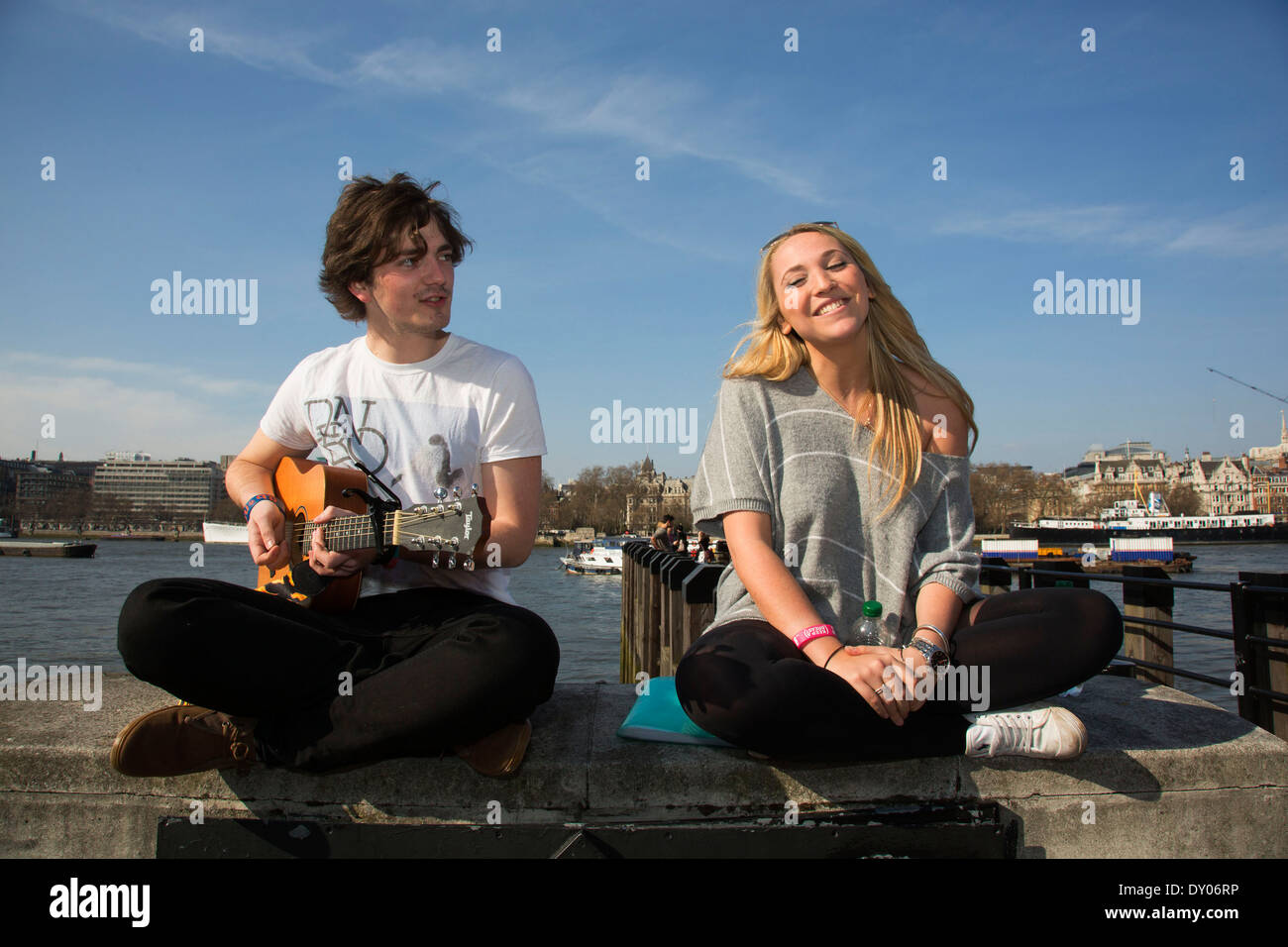 Two young buskers singing and playing guitar on the riverside wall ...