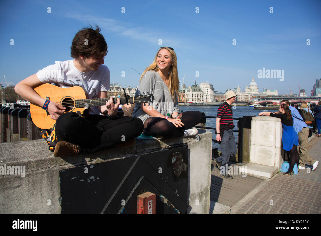 Two young buskers singing and playing guitar on the riverside wall ...