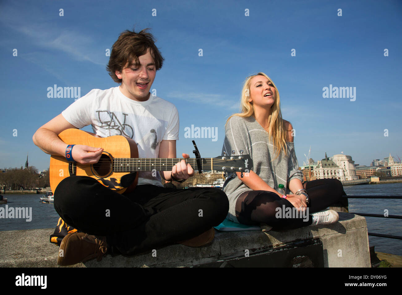 Two young buskers singing and playing guitar on the riverside wall ...