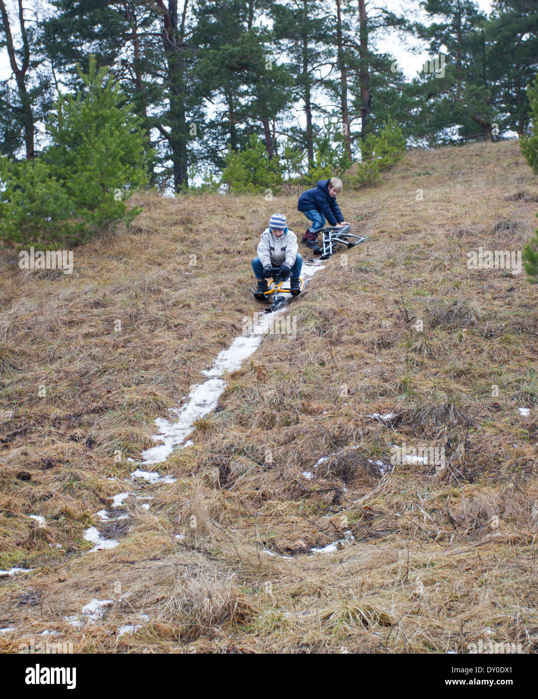 Two boys trying their snow racers on a hill with very little snow on ...