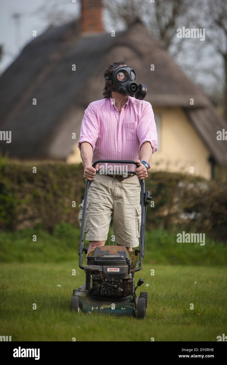 Arkesden, Essex . Man mowing the lawn wearing a gas mask as a ...