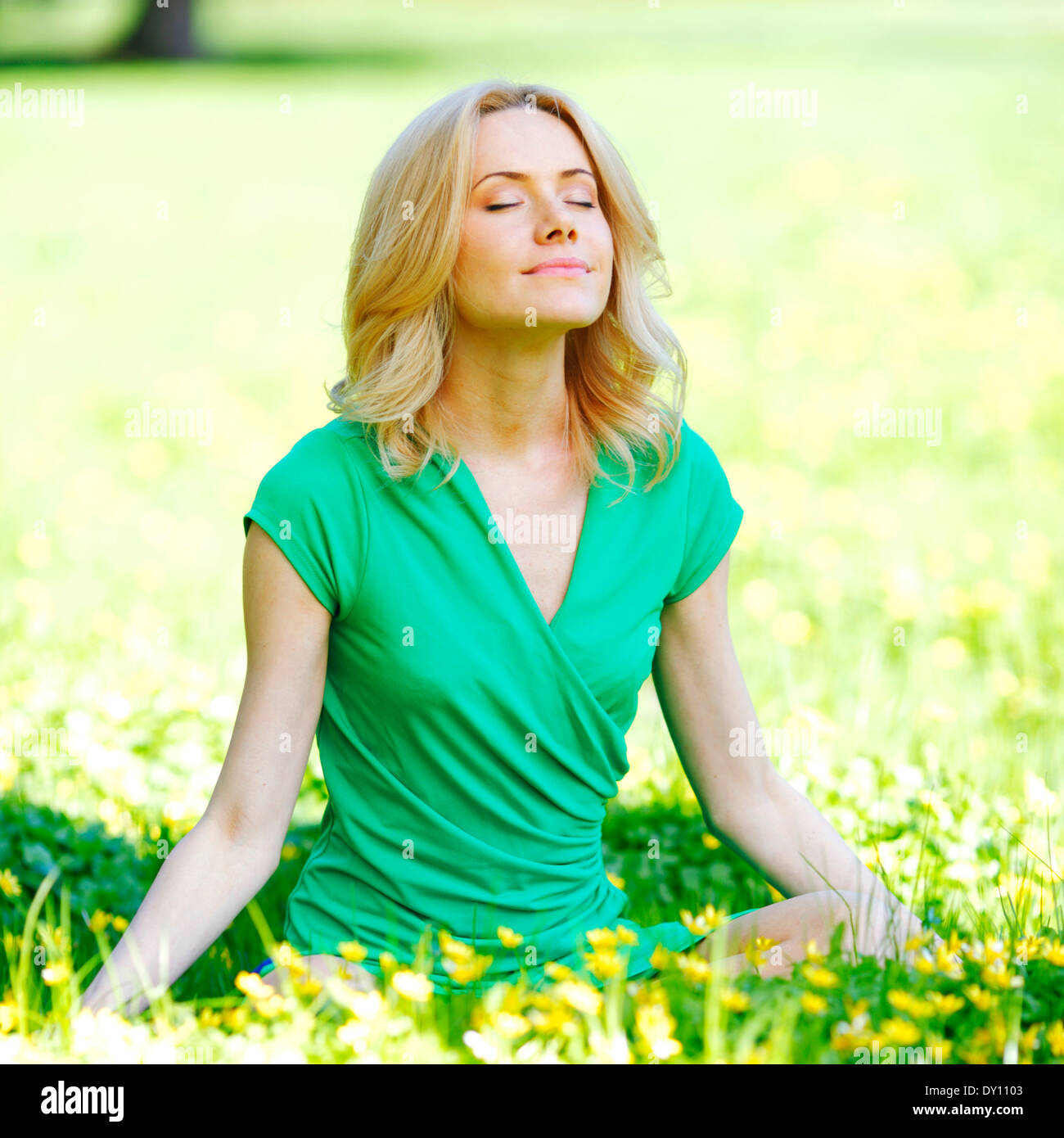 Beautiful young woman sitting on flower field in lotus pose Stock Photo ...