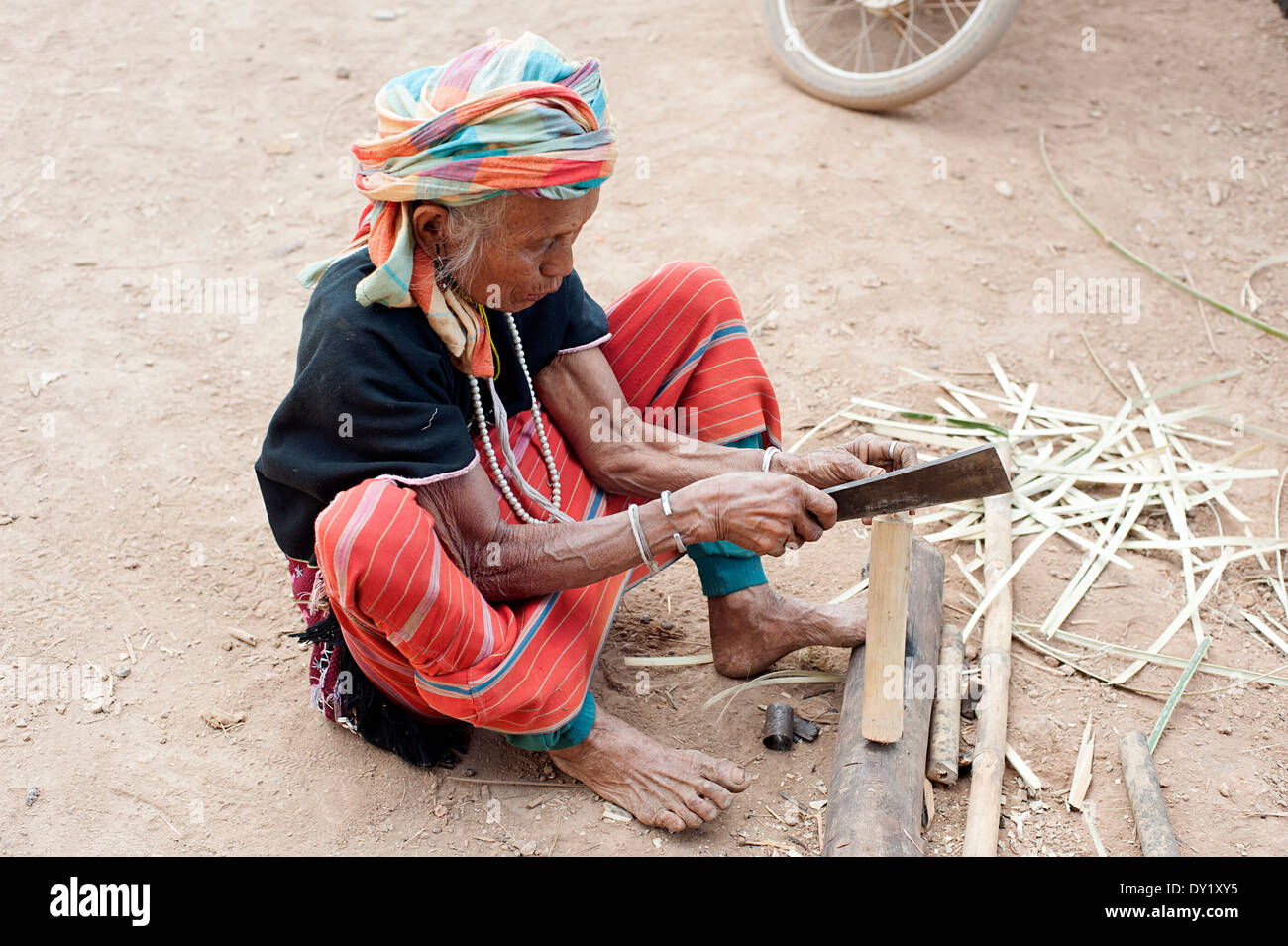 Elderly Karen woman sits on the ground using a machete to chop a piece ...