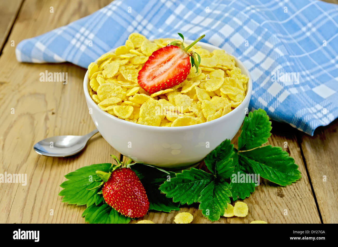 Cornflakes in a white bowl with half a strawberry, leaves and ...
