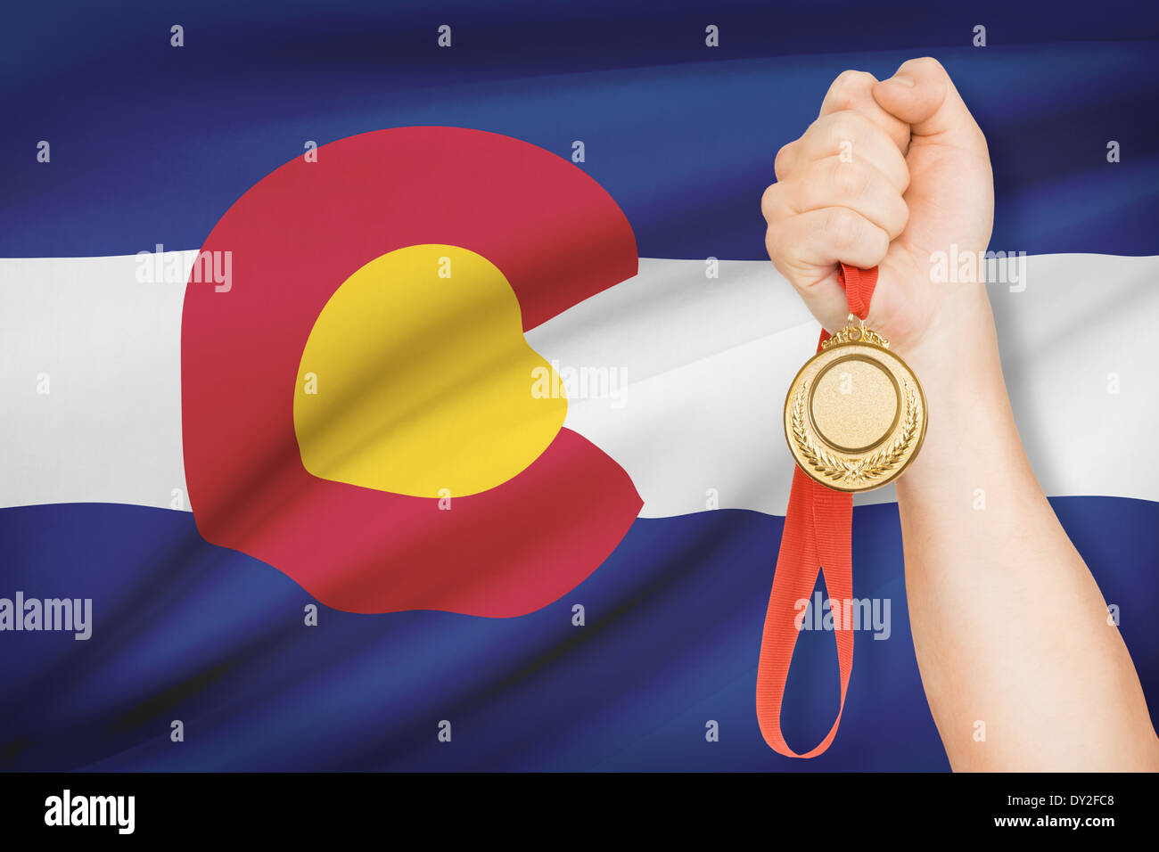 Sportsman holding gold medal with State of Colorado flag on background ...