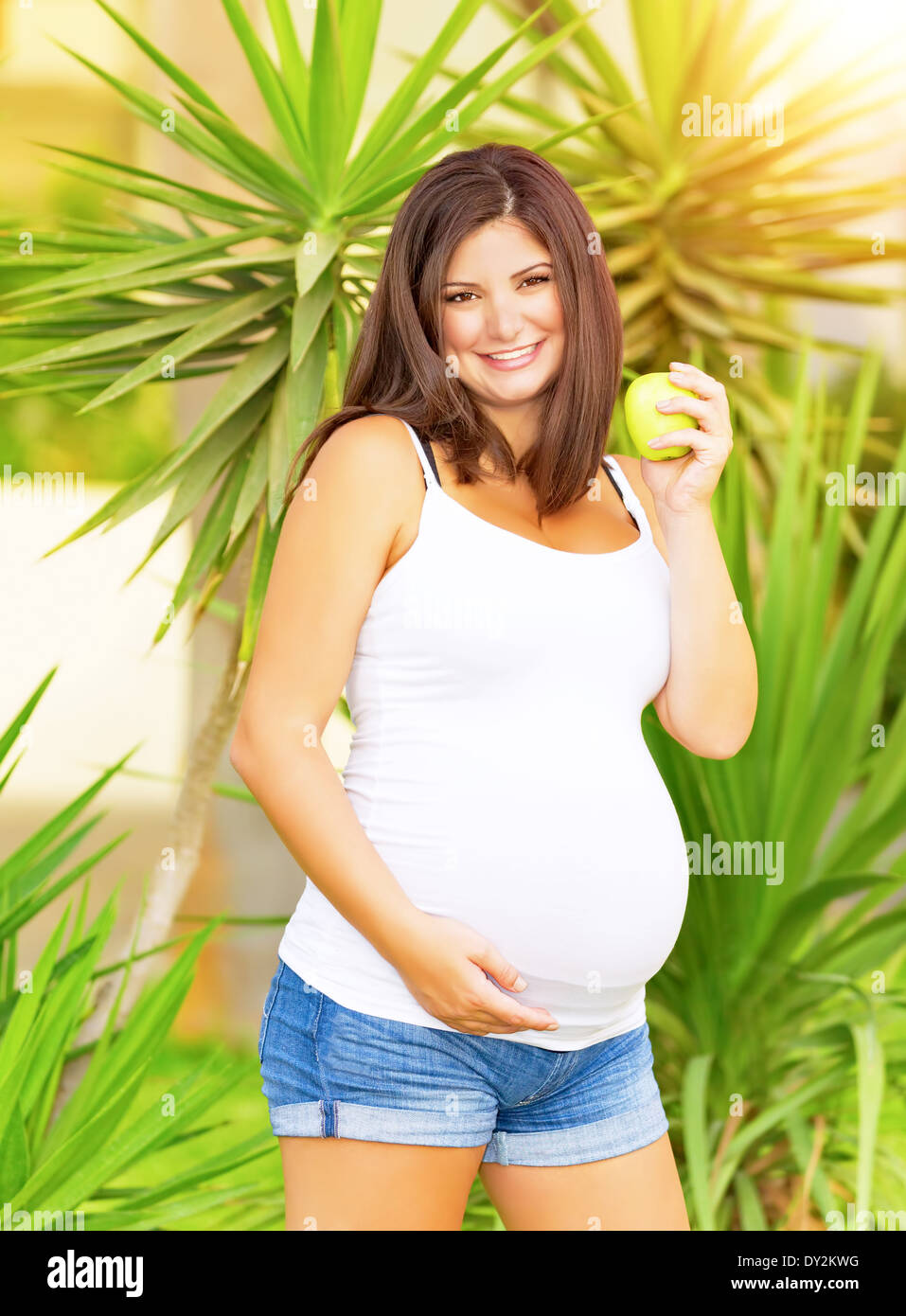 Portrait of cheerful expectant girl eating fresh tasty apple fruit ...