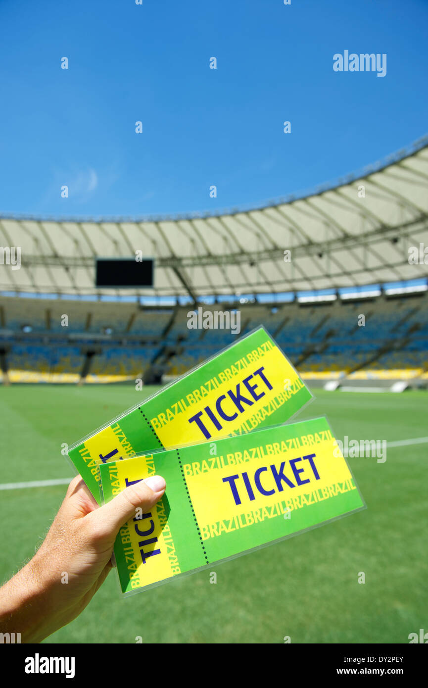 Soccer fan holding two tickets in front of a bright football pitch in ...