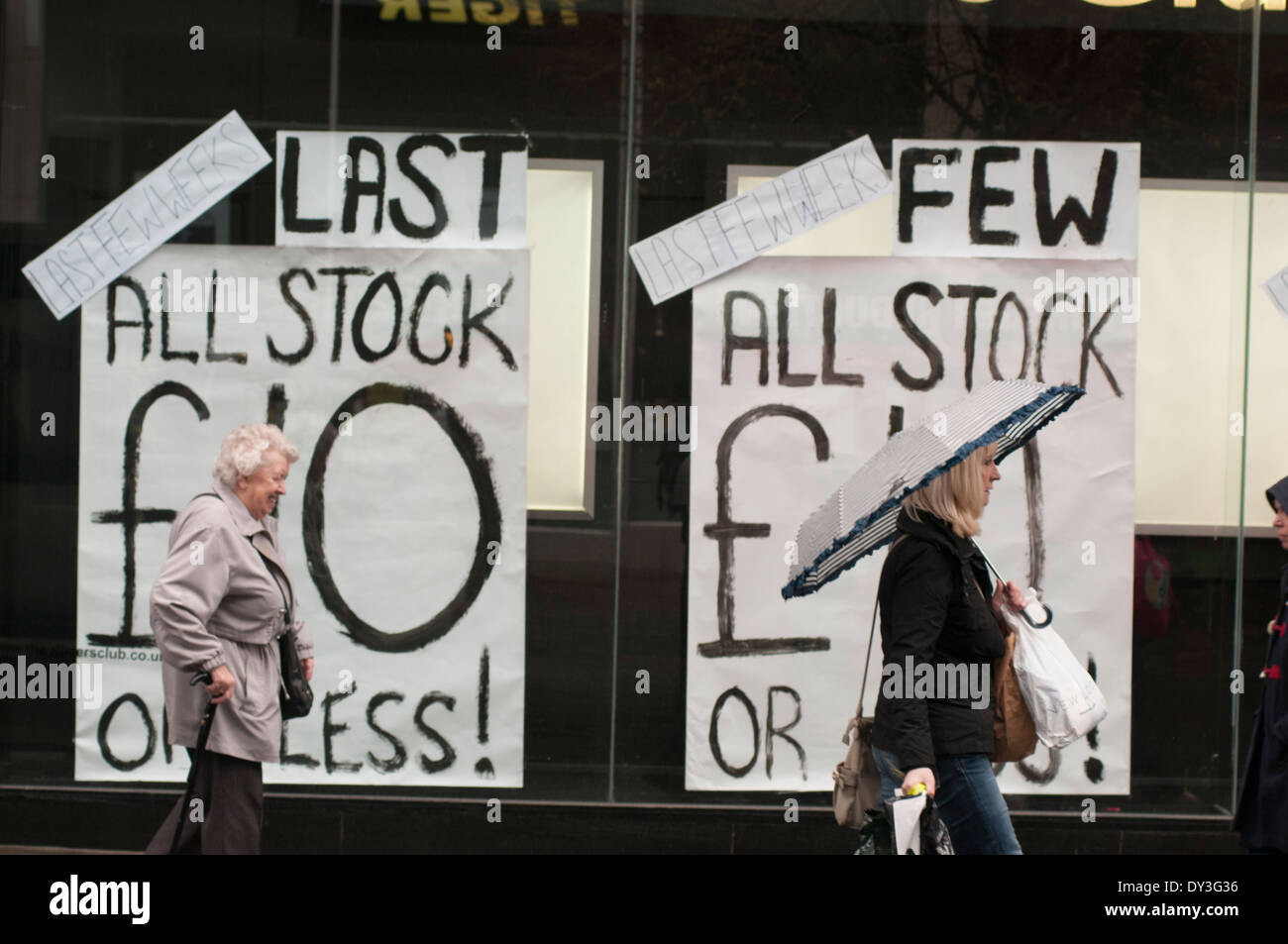 Shop closing down sale signs in a shop front with people walking past ...