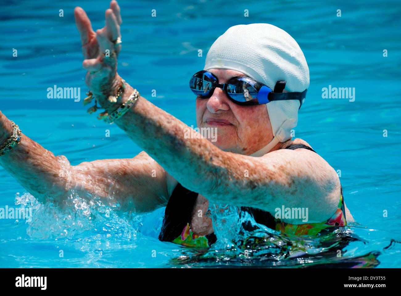 A senior citizen woman in a bathing suit, swim cap and goggles enjoys a ...