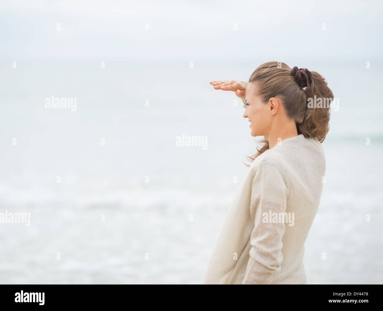 Young woman looking into distance while standing on cold beach standing ...