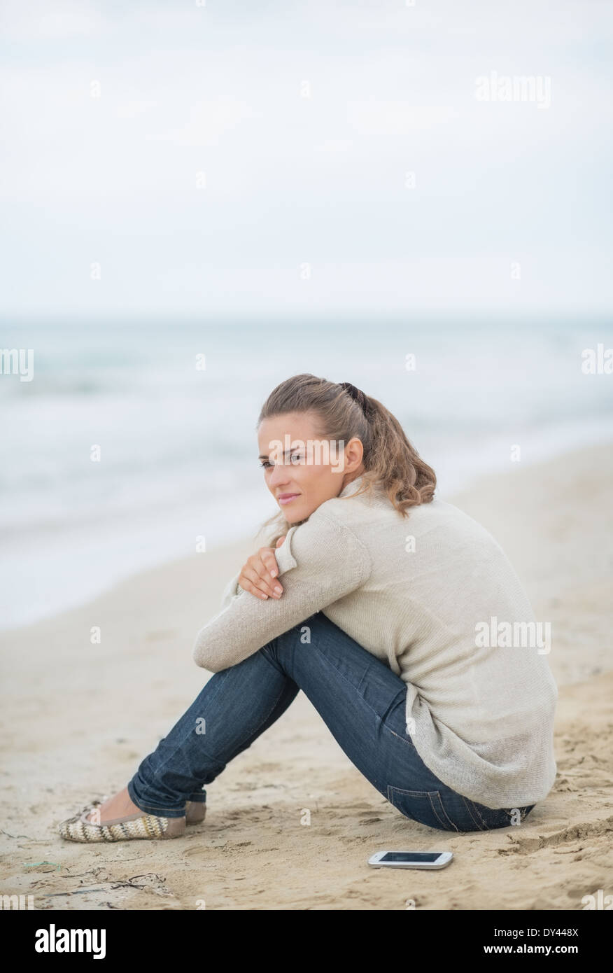 Calm young woman sitting on cold beach Stock Photo - Alamy