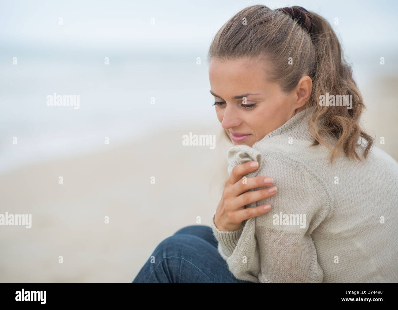 Portrait of calm young woman sitting on cold beach Stock Photo - Alamy