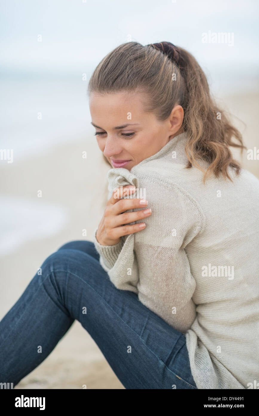 Calm young woman sitting on cold beach Stock Photo - Alamy
