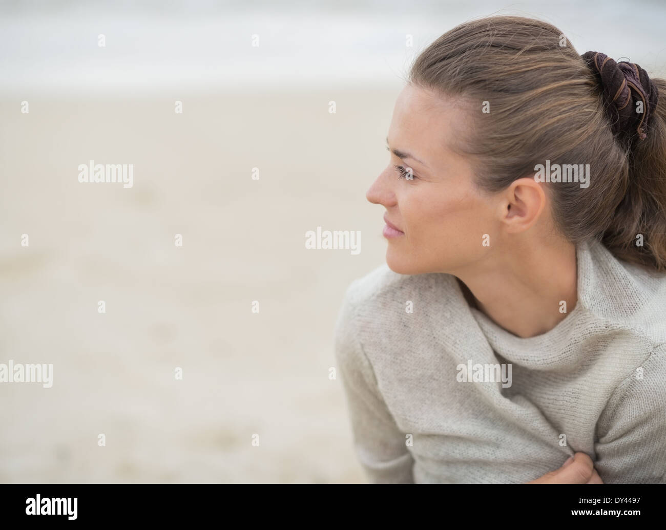 Calm woman sitting on cold beach and looking into distance Stock Photo ...