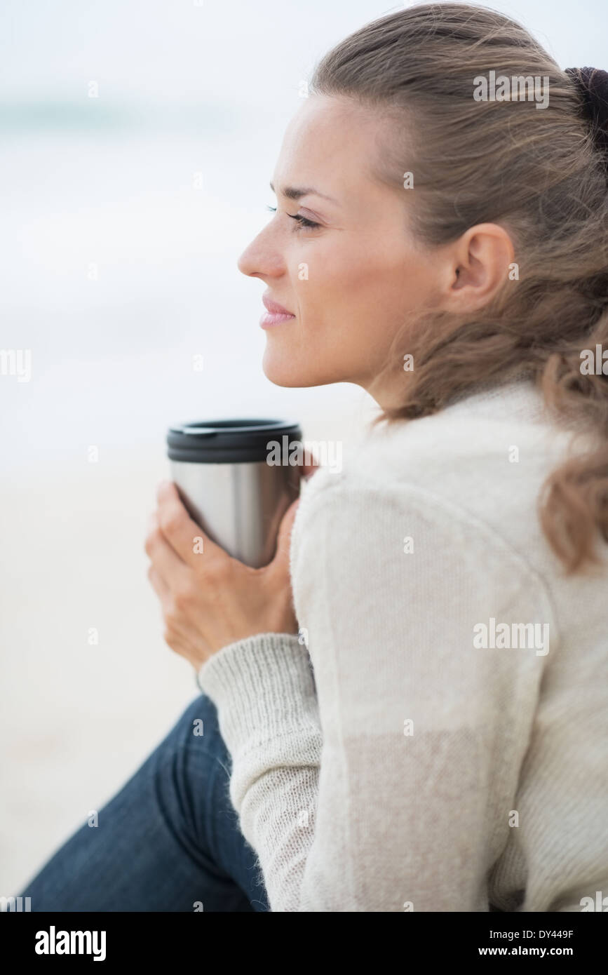 Calm woman sitting on cold beach with cup of hot beverage Stock Photo ...