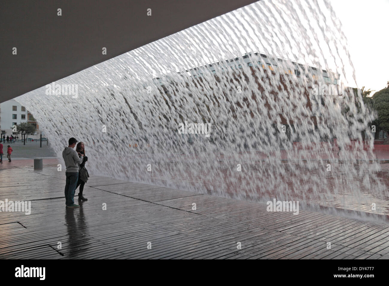 A couple walk under a waterfall (the water continuously falls over the ...