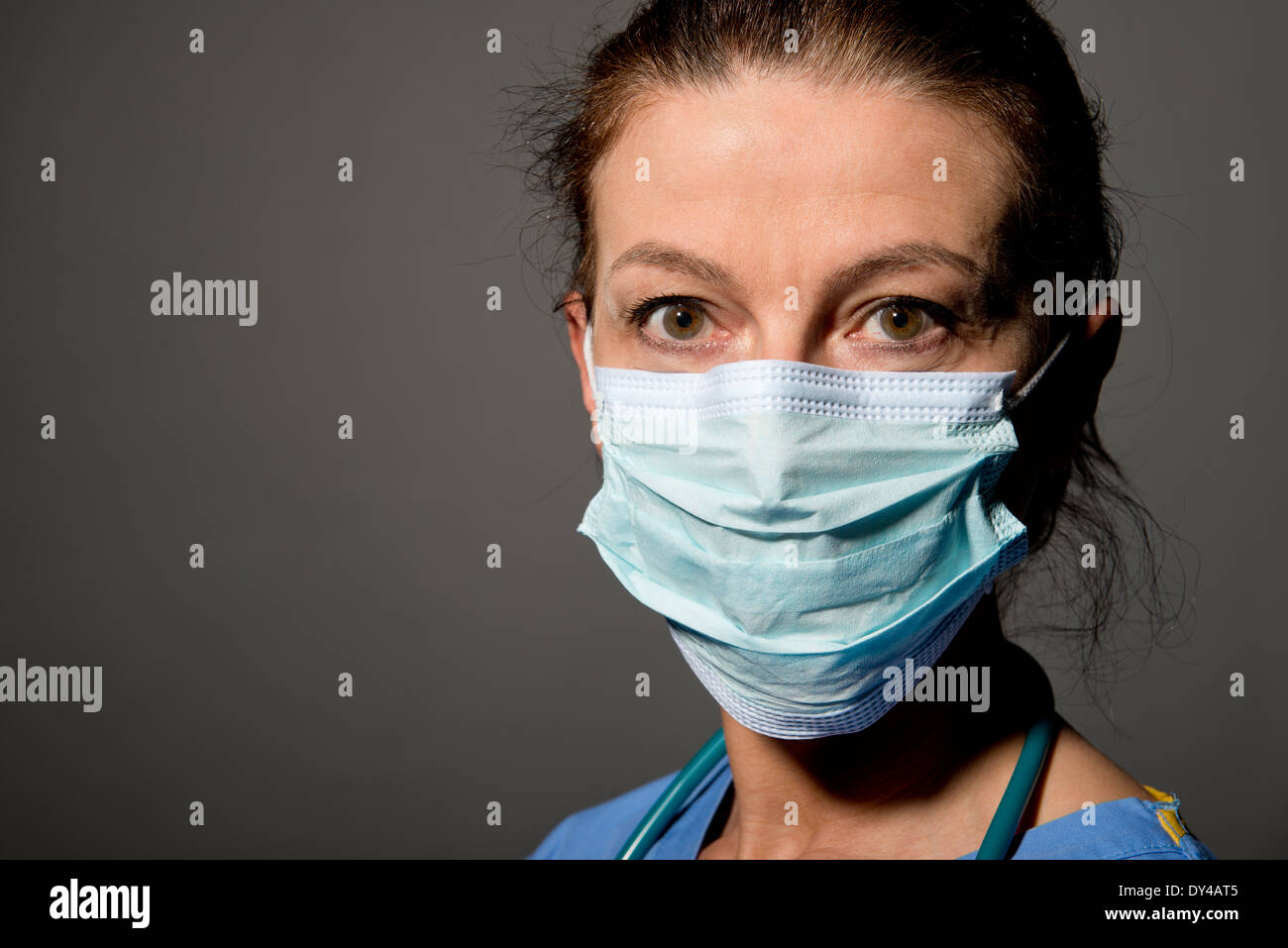 Tired looking nurse/doctor wearing a blue surgical mask, against a grey ...