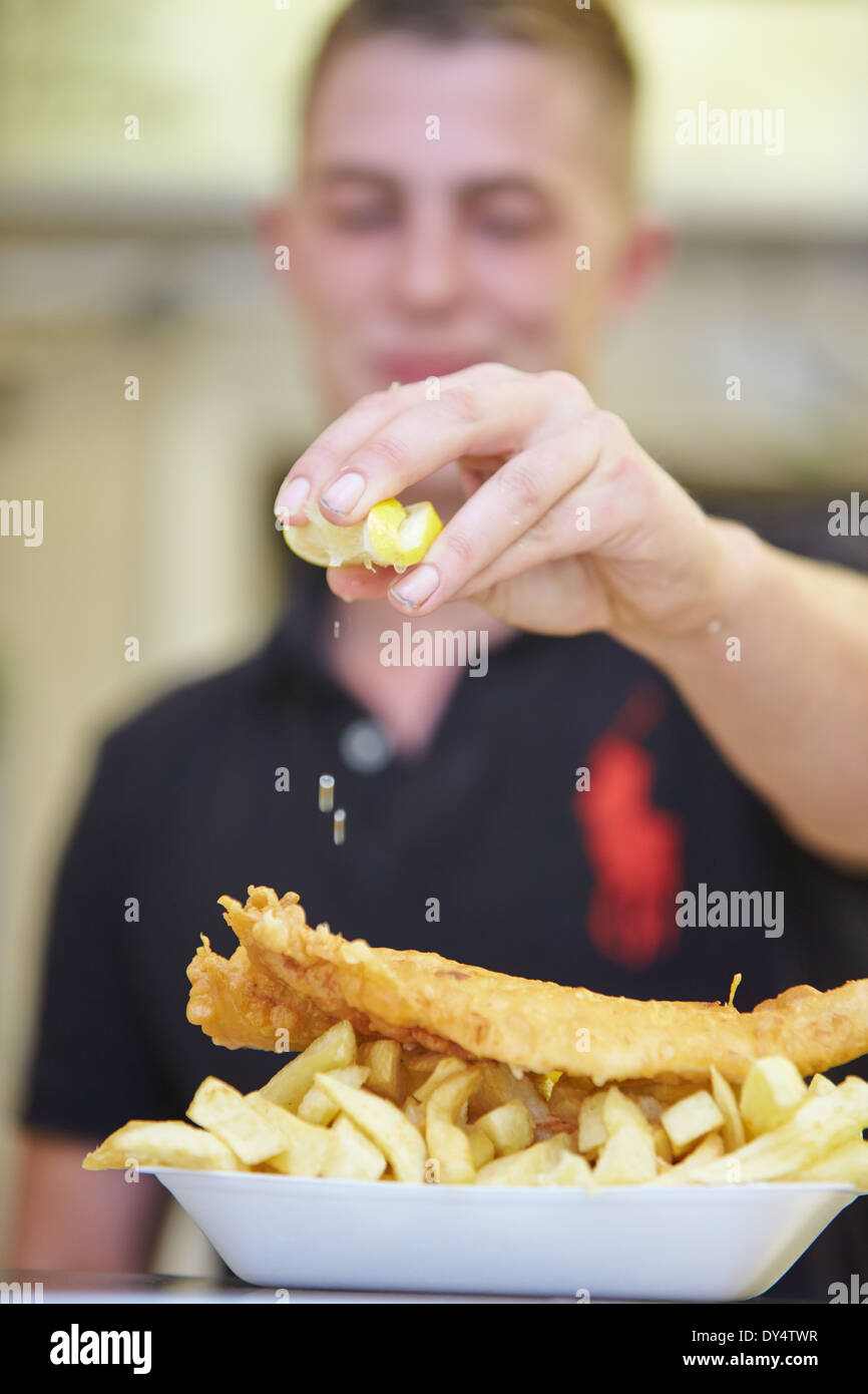 Staff member squeezing a lemon slice over a battered fish and chip ...