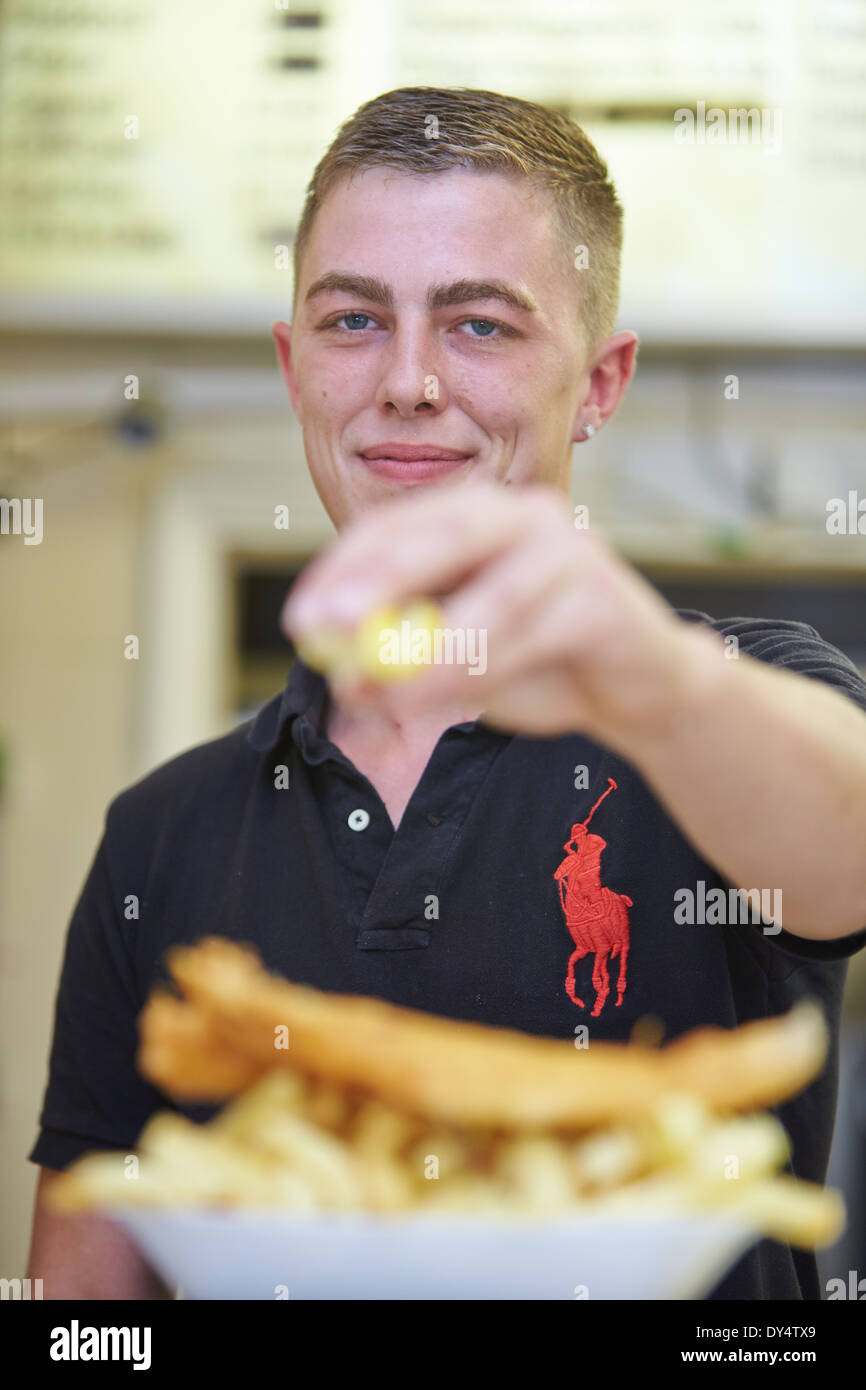Staff member squeezing a lemon slice over a battered fish and chip ...