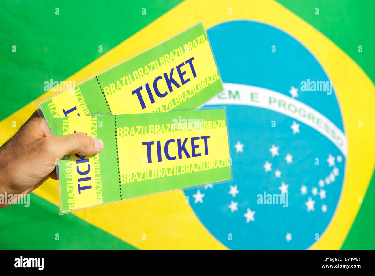 Hand holding two Brazil tickets against bright Brazilian flag ...
