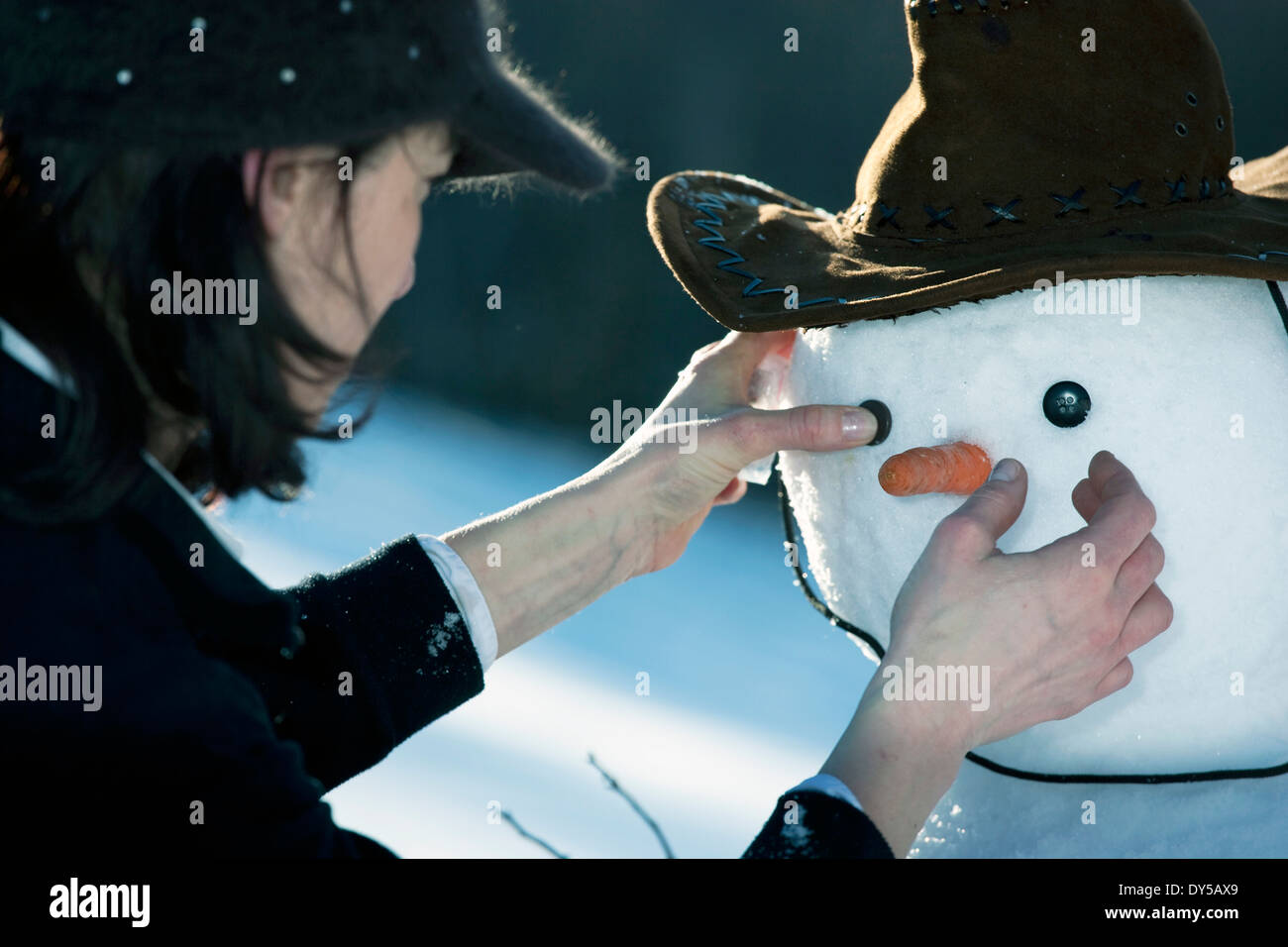 Mature woman placing the eyes on a snowman face Stock Photo - Alamy