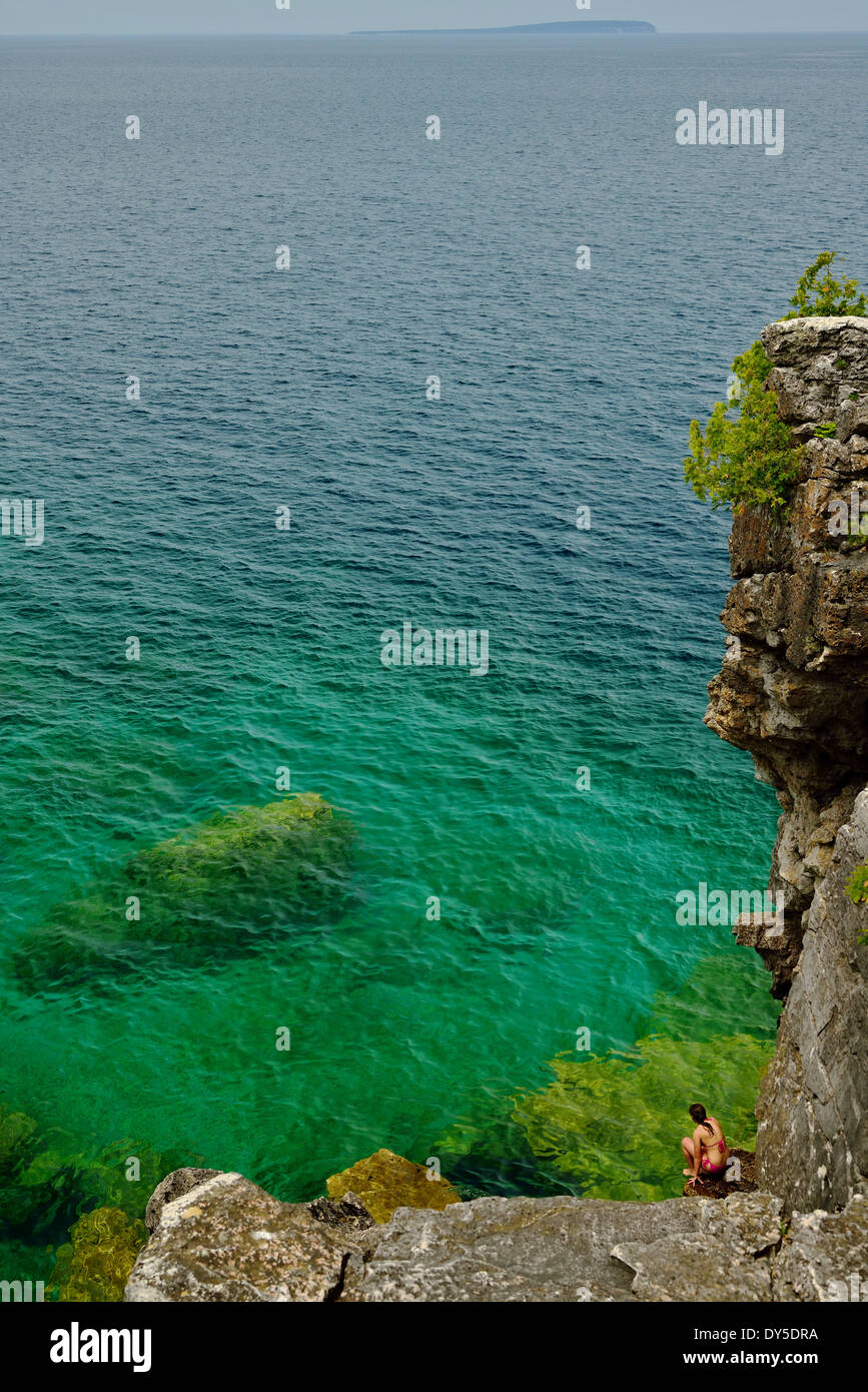 Mid adult woman crouching on rocks at coast, Toronto, Ontario, Canada ...