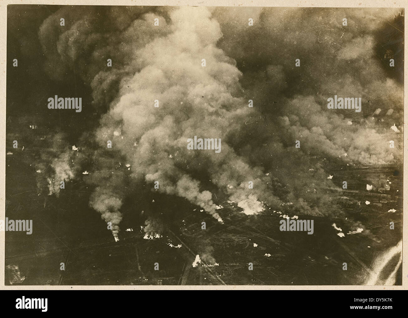 The aerial image shows a munitions factory on fire, with smoke rising ...