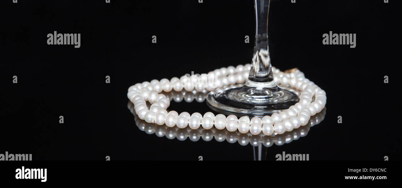 A strand of beautiful pearls sit around the base of a glassware stem on ...