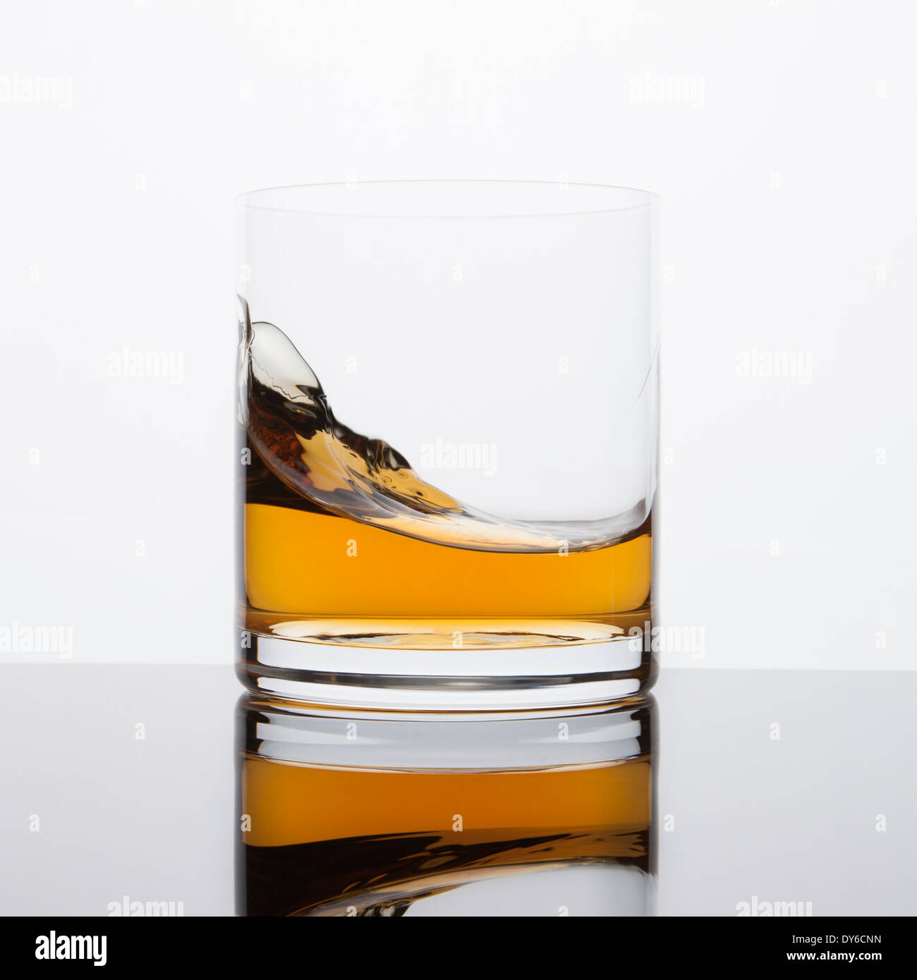 A rocks glass with Whisky sits atop a reflective surface on a bright ...
