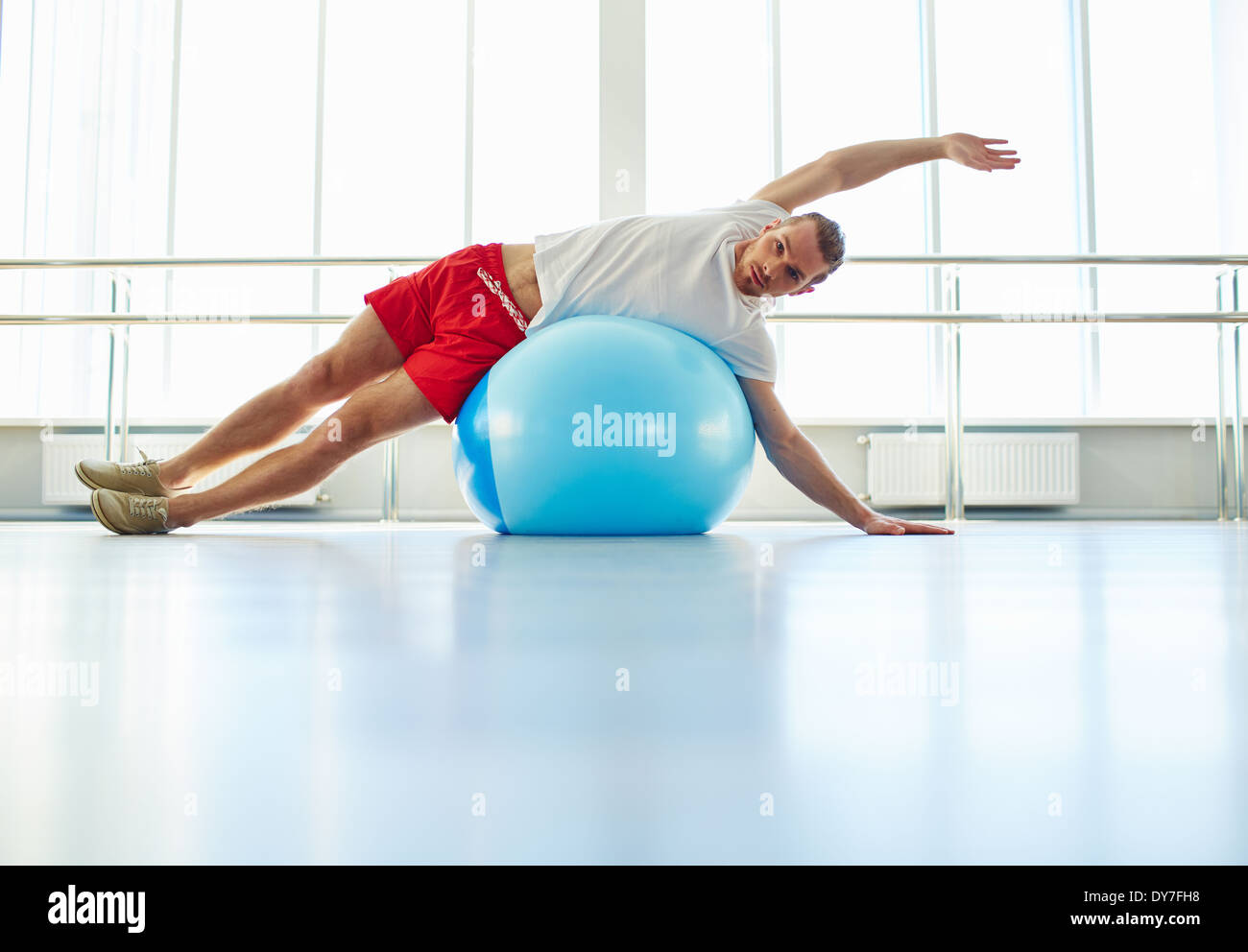 Portrait of young man doing physical exercise on ball and looking at ...