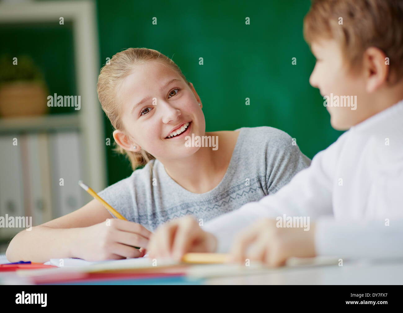 Image of cute girl with pencil looking at camera while talking to her ...